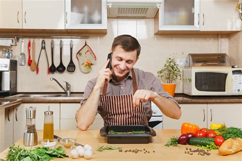 앞치마 야채와 함께 테이블에 앉아 있는 젊은 남자 나무 표면 멋진 주방의 전체 빛 부엌에 쇠고기 또는 양고기 고기 스테이크를 준비 하는 가정에서 요리 휴대 전화에 대 한