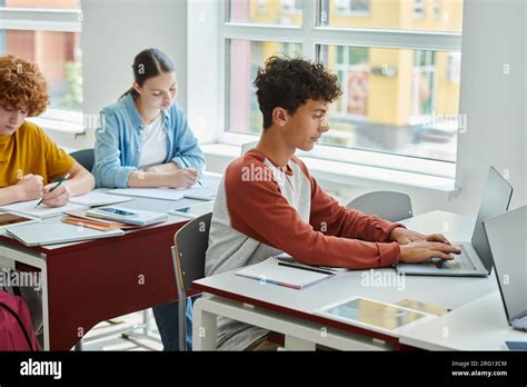 Teenage Babebabe Using Laptop Near Notebooks And Blurred Classmates In Classroom In Babe