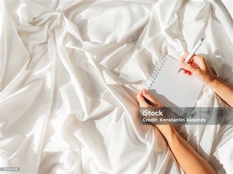 여자는 일기에 쓰거나 그릴 준비를하고 있습니다 구겨진 침대 시트와 흰색 종이 페이지가있는 메모장의 상단 보기 깨어난 후 아침에 긍정적 인 글쓰기 연습 복사 공간이 있는 플랫