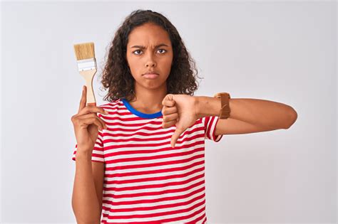 화가 얼굴 엄지 손가락으로 싫어하는 것을 보여주는 부정적인 기호 거부 개념으로 고립 된 흰색 배경 위에 서 브러시를 들고 젊은 브라질 화가 여자 Diy에 대한 스톡 사진 및