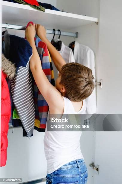 옷을 입고 옷장 옆에 서 있는 학교 아이 소년 학교 셔츠 착용에 대한 결정을 내리는 어린이 아이들은 아침에 학교에서 옷을 입습니다 아이에 대한 스톡 사진 및 기타 이미지