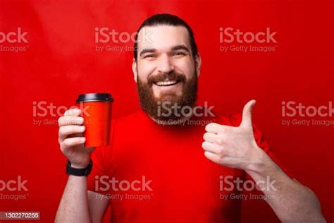 엄지 손가락을 보여주고 커피의 빨간 종이 컵을 들고 수염을 가진 매력적인 젊은 남자 테이크 아웃 25 29세에 대한 스톡 사진 및 기타 이미지 Istock