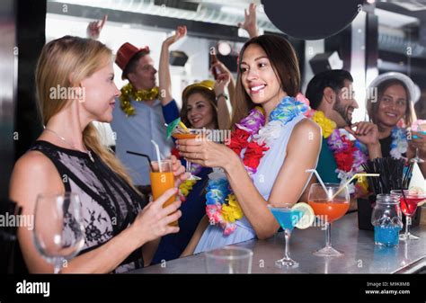 Two Smiling Female In Lei Are Drinking Cocktails On Hawaiian Party