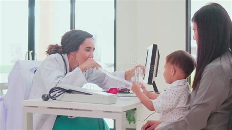 Female Pediatric Doctor Teasing Boy With Toy For Medical Examination