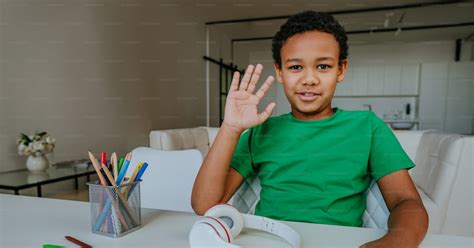 집에서 온라인 수업 중에 손을 흔들고 인사하는 카메라를 보는 소년의 초상화 사진 Unsplash의 남학생 이미지