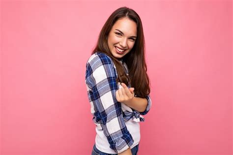 트렌디 한 파란색과 흰색 셔츠에 젊은 아름다운 미소 힙스터 갈색 머리 여자의 사진 초상화 스튜디오의 빈 공간이있는 분홍색 벽 근처에서 고립 된 포즈를 취하는 섹시한 평온한