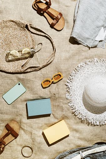 패션 여름 해변 휴식 컨셉 캐주얼 옷 세련된 비치 백 블루 파나마 샌들 건강한 레몬 워터 스마트폰 책 바다에서 휴식을 취하는 현대 여성의 액세서리 빈티지 톤 샌들에 대한