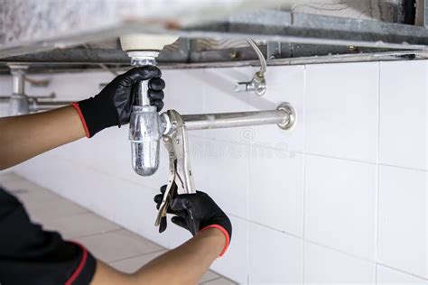 technician plumber using a wrench to repair a water pipe under the sink