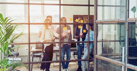 사업 아이디어 공유 회의실의 유리 벽 뒤에 서서 접착 노트를 사용하는 스마트 캐주얼 웨어를 입은 젊은 현대인의 전체 길이 사진 Unsplash의 팀워크 이미지