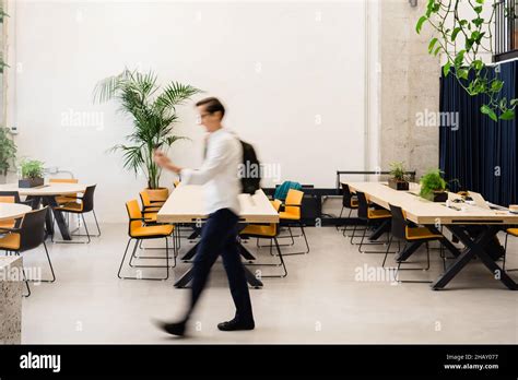 Full Body Side View Of Blurred Male Worker With Backpack Strolling In Light Modern Workspace
