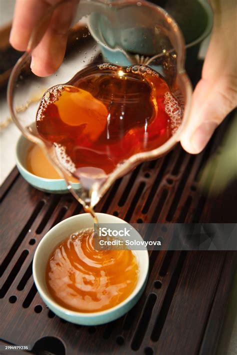 투명한 유리 주전자에서 찻잔에 담긴 차를 따르는 여성의 손은 고요한 차 의식을 만듭니다 부드러운 빛 나무 찻 트레이는 차분한 마음 챙김 Chenese 의식 분위기를 불러