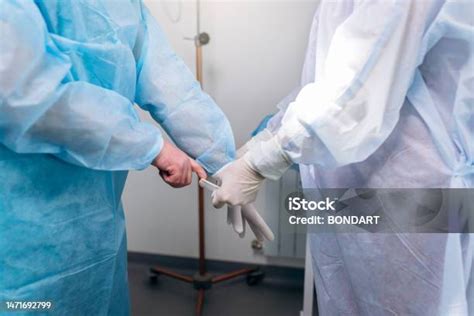 수술 전에 외과의에게 의료용 장갑을 끼고 있는 간호사의 클로즈업 의사는 수술실에서 수술을 준비하고 의료 유니폼을 입습니다 2명에