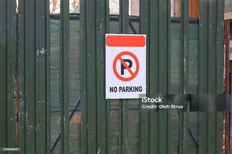 사진은 녹색 금속 울타리에 부착된 주차 금지 표지판을 보여줍니다 표지판은 흰색 배경에 빨간색 원이 그어져 있고 문자 P와 아래에 No Parking이라는 비문이 있습니다 0