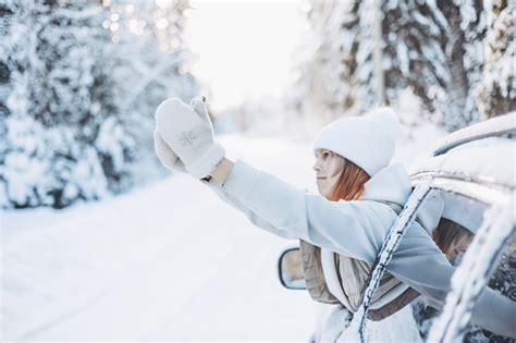 겨울 눈 덮인 숲에서 자동차 창문을 바라보고 스마트 폰에서 셀카를 찍는 십대 소녀 도로 여행 및 지역 여행 개념 자동차 타기를