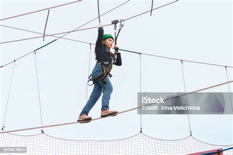 등반 하네스 장비 녹색 스포츠 안전 헬멧을 쓴 십대 소녀 로프 놀이 공원 카라비너를 안전 로프에 부착하는 고정 매달린 장애물 코스 어린이 어린이 명소 8 9 살에 대한 스톡