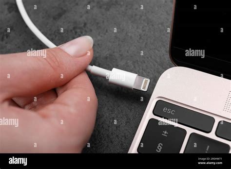 Woman Plugging USB Cable With Lightning Connector Into Laptop Port On Dark Table Closeup Stock