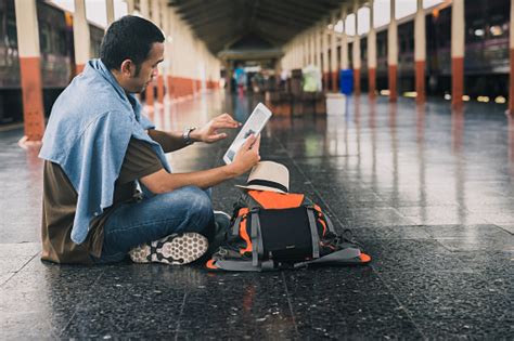 기차역 바닥에 앉아 디지털 태블릿을 가진 젊은 남자 여행자가 어디로 갈지 선택합니다 배낭 여행자의 개념은 기차로 모험을 여행합니다 40 44세에 대한 스톡 사진 및 기타
