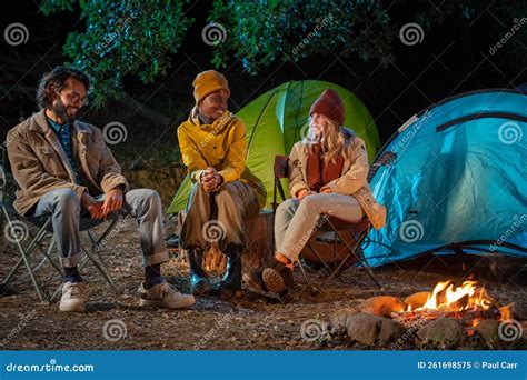 Three Happy Friends Enjoying Camping With Tent Chatting By A Fire
