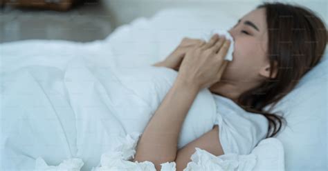 잠옷을 입은 아시아 아픈 소녀는 침대에서 재채기를 하는 밤에 잠에서 깨어난다 기분이 좋지 않고 알레르기로 고통받는 매력적인 젊은 여성은 집에서 취침 시간 동안 재채기를하는