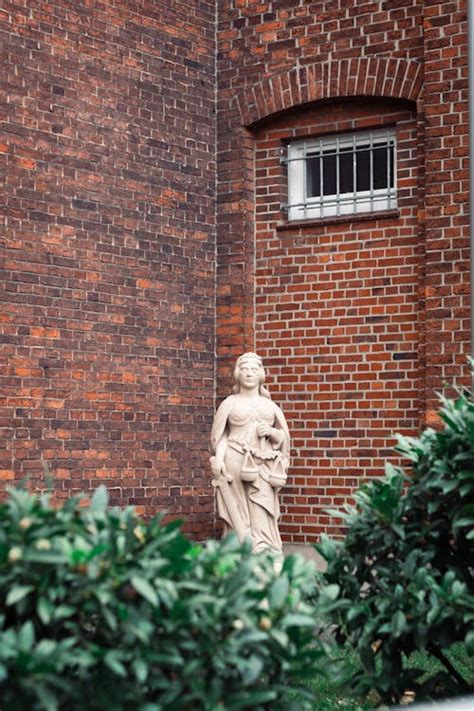 붉은 벽돌 벽 옆에 있는 정의의 여신상 · 무료 스톡 사진