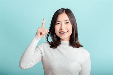 하얀 이빨로 중괄호를 입은 젊은 아시아 여성의 치과 중괄호는 파란색 배경 고립 된 스튜디오 샷 복사 공간으로 충격과 기쁜 프로모션에 대한 자신감을 증가시다 20 29세에