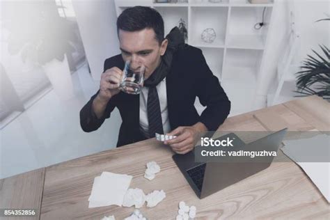 아픈 남자는 사무실에서 그의 직장에서 앉아 있다 그는 그의 손에 알 약과 물 컵 감기와 독감에 대한 스톡 사진 및 기타 이미지 감기와 독감 건강관리와 의술 건강한