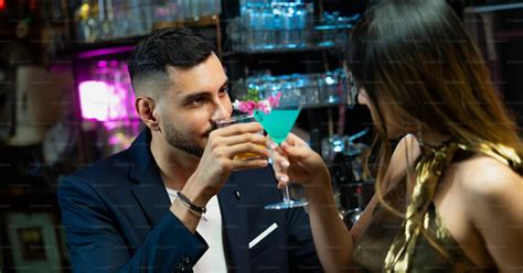 아시아 여성은 바 카운터에 서서 나이트클럽에서 알코올 칵테일을 마시며 남자친구와 이야기를 나눈다 남성 바텐더 믹솔로지스트는 바 카운터에서 칵테일 잔을 장식하여 혼합 알코올