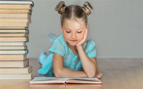 어린 여학생은 바닥에 누워 미소를 지으며 책을 읽습니다 흐릿한 밝은 배경에 책의 스택 근처 학교 개념으로 돌아갑니다 공간을 복사합니다 소녀에 대한 스톡 사진 및 기타 이미지