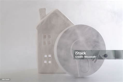 백색 배경에 고립 된 두꺼운 연기로 둘러싸인 일반 연기 감지기 및 미니어처 하우스로 화재 예방 가정 보안 및 위험한 연기 개념 적 아이디어 모니터링 연기 탐지기에 대한 스톡