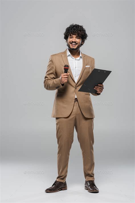 Full Length Of Smiling Indian Event Host In Brown Formal Wear Holding
