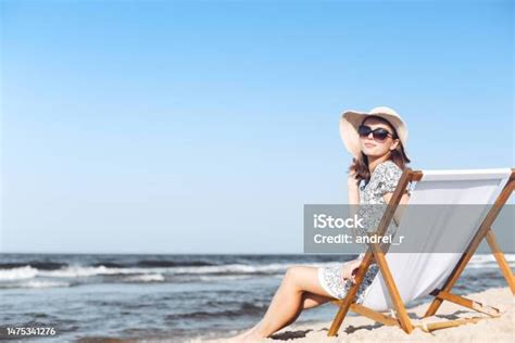 선글라스와 모자를 쓰고 바다 해변의 나무 갑판 의자에서 휴식을 취하는 행복한 갈색 머리 여자 25 29세에 대한 스톡 사진 및 기타 이미지 Istock