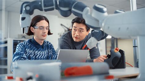 다민족 사무실의 팀워크 프로젝트 관리자는 랩톱 컴퓨터에서 작업하는 동료를 지원합니다 전문가들은 로봇 팔을위한 프로그램을 만듭니다 자동화된 로봇 시스템을 설계하는 사람들 공장