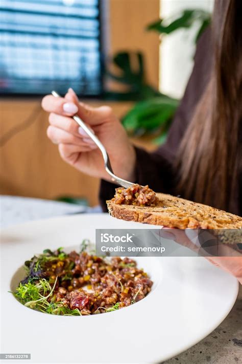 고명을 곁들인 미식가 타르타르 요리의 클로즈업 토스트를 손에 들고 먹는 여자 우아한 표현 생생한 색상 신선한 재료 요리 식사 및 라이프스타일 테마에 이상적입니다 건강한