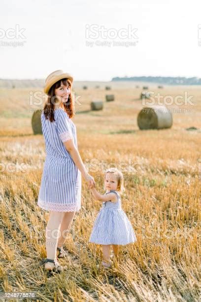 행복한 어머니와 어린 아기 유아 소녀는 손을 잡고 배경에 건초 베일과 여름 수확 필드를 통해 걷는 동안 재미를 여름 일몰 가족 산책 현장 2명에 대한 스톡 사진 및 기타