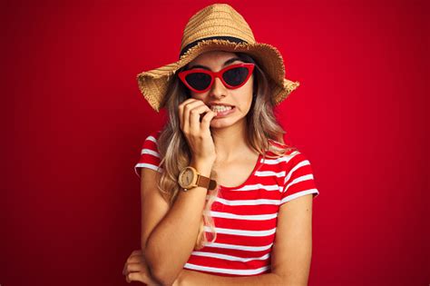 젊은 아름다운 여성은 선글라스와 여름 모자를 입고 빨간색 고립 된 배경 위에 스트레스와 긴장 을 찾고 입물고 손톱에 손을 불안 문제 열 개념에 대한 스톡 사진 및 기타