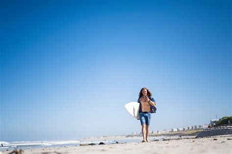 그의 휴대 전화를 확인 해변에서 서핑 보드와 함께 걷는 미소 남성 서퍼 20 24세에 대한 스톡 사진 및 기타 이미지 20 24세 Brand Name Smart