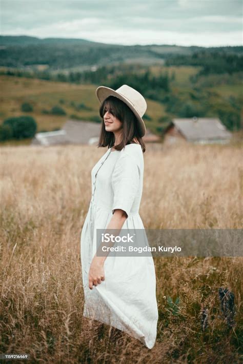 밭에서 허브와 야생화 사이를 걷는 린넨 드레스와 모자를 입은 세련된 소녀 시골에서 미소와 휴식 간단한 느린 생활 스타일 텍스트의 공백입니다 대기 이미지 드레스에 대한 스톡