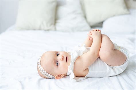 하얀 면 바디수트를 입은 귀여운 아기가 웃거나 다리를 가지고 놀고 웃고 있다 보육원에서 집에서 가벼운 침대에 누워 있는 아기 소녀 클로즈업 2 5 개월에 대한 스톡 사진 및