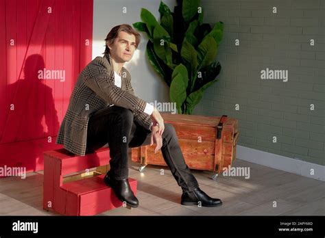 Tall Handsome Man Sitting On The Red Stairs Next To Green Plant And