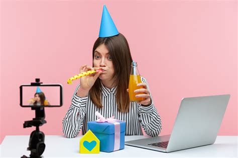 원뿔 모자에 재미 여자 불고 파티 송풍기 에 레모네이드와 병을 들고 스마트 폰 카메라에 비디오 축하를 녹화 선물을 준비 25