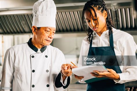 전문 아시아 선임 셰프가 레스토랑 주방에서 다양한 학생들을 가르칩니다 팀워크 학습과 메모 작성을 강조합니다 교육 워크숍이 진행 중입니다 음식 도크 요리사에 대한 스톡 사진