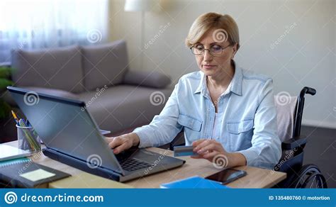 Nice Senior Woman In Wheelchair Typing Card Number On Laptop Paying