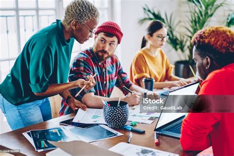 종이 문서 및 노트북 앱과의 브레인스토밍 협력 중 스타트업을 개발하는 다인종 남녀 직원 데스크톱에서 교육 정보를 논의하는 다양한 전문가 20 24세에 대한 스톡 사진 및