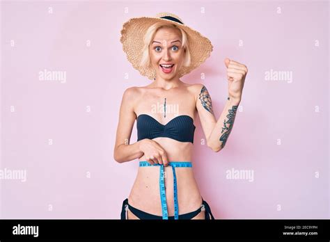 Young Blonde Woman With Tattoo Wearing Bikini Using Tape Measure