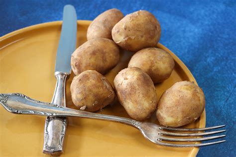 스테인레스 스틸 나이프와 포크가 시계 문자판과 바늘을 형성하는 노란색 접시의 전체 프레임 이미지 작은 섹션의 감자 더미 파란색 배경 높은 전망 다이어트 및 간헐적 단식 개념