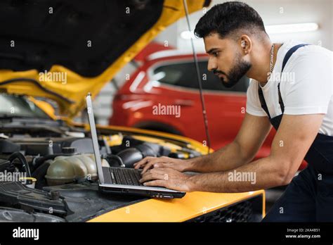 Young man car mechanic maintains vehicle using diagnostic laptop ...