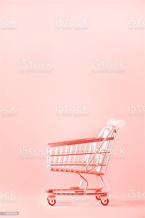 트렌디 한 산호 색상 배경에 쇼핑 카트입니다 미니멀리즘 스타일 창의적인 디자인 공간을 복사합니다 슈퍼마켓에서 트롤리를 쇼핑하세요 판매 할인 쇼핑 중독 개념 소비자 사회 동향