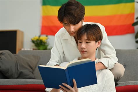 행복한 게이 커플은 집에서 소파에 앉아 책을 읽고 주말에 함께 시간을 보낸다 Lgbtq 사람들의 라이프 스타일과 사랑 감정 20 24세에 대한 스톡 사진 및 기타 이미지