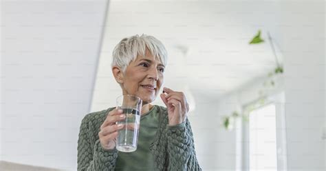 거실의 소파에 앉아 진통제약을 복용하고 있는 질병 증상을 완화하는 웃는 숙녀 사진 Unsplash의 약 이미지