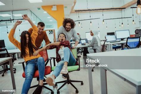 팀 빌딩과 사무실의 즐거움 똑똑한 캐주얼 옷을 입은 젊은 쾌활한 사업가들은 사무실 의자에서 경주하고 웃으며 즐거운 시간을 보내고 있습니다 긍정적인 감정 표현에 대한 스톡